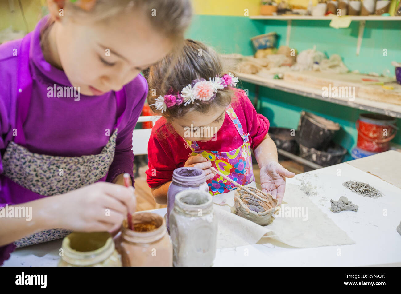 Two little young artist girl painting with brush clay vase at table in ...