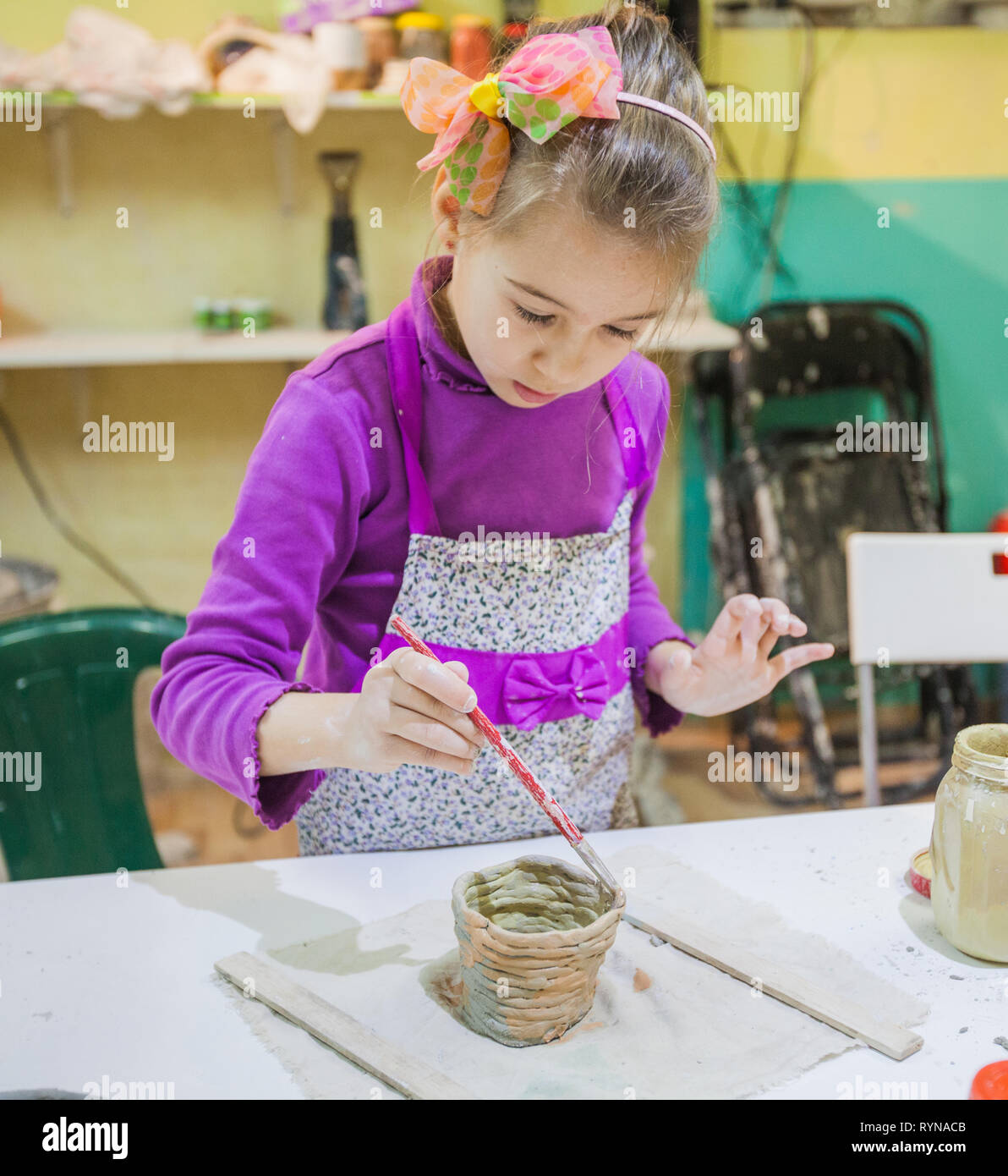 little girl in ceramic studio painting self-made clay vase on table at ...