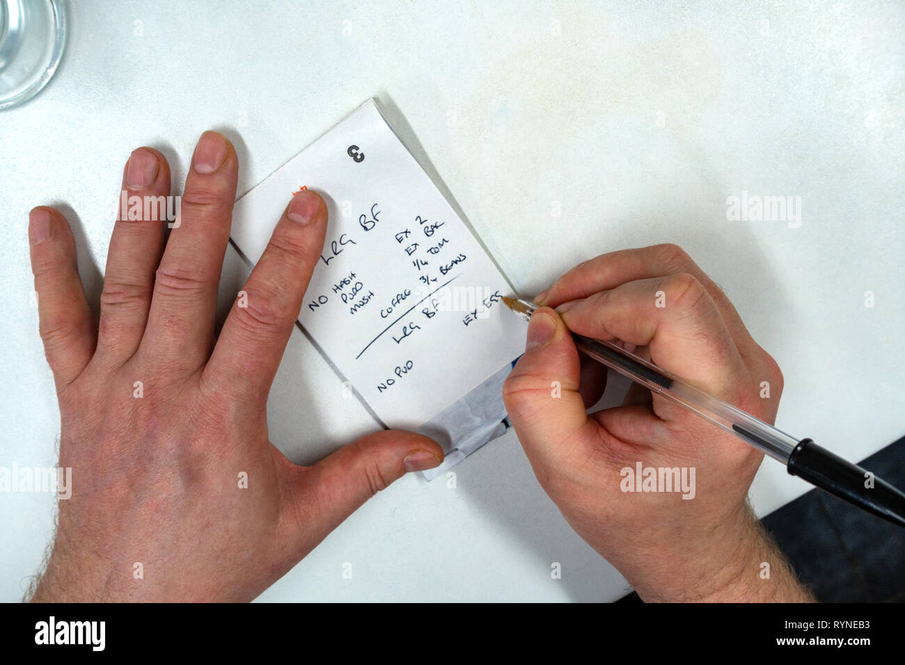 Close up photograph of a waiter's hands writing on order pad and taking ...