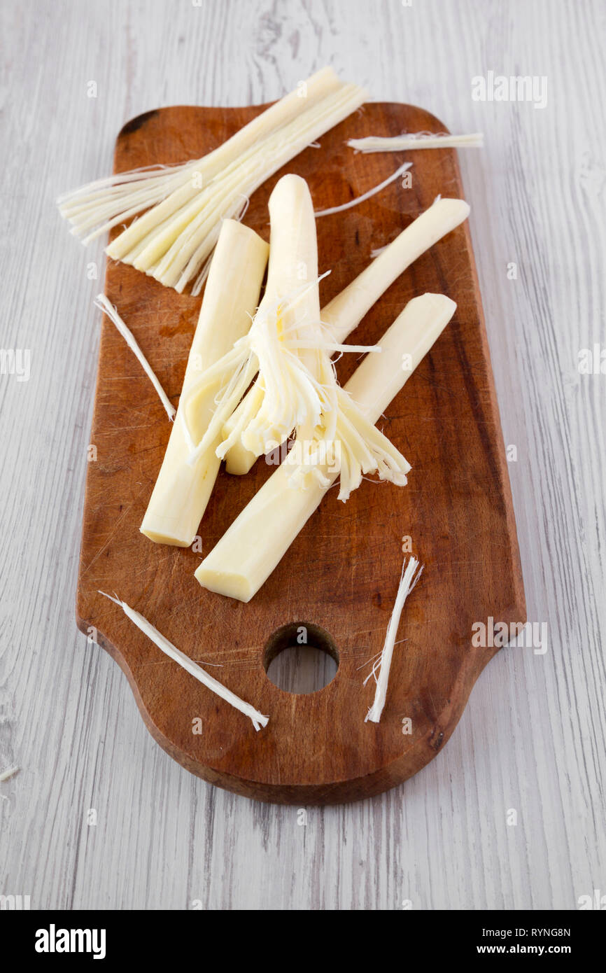 String cheese on rustic wooden board over white wooden surface, side ...
