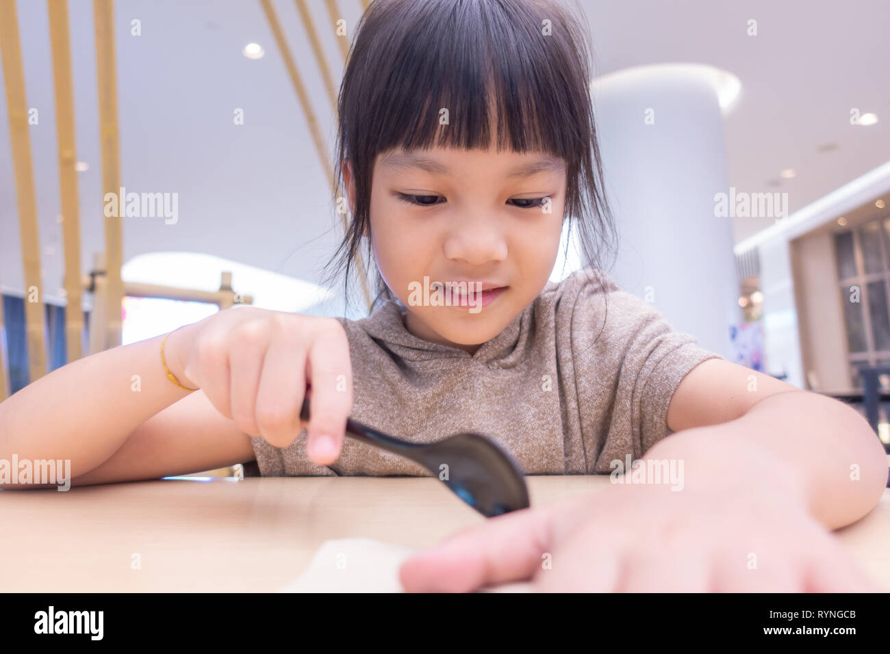 Asian kid using spoon to eat food in restaurant Stock Photo - Alamy