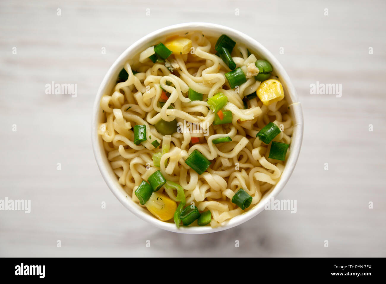 A paper cup of instant ramen noodles over white wooden surface. Flat ...