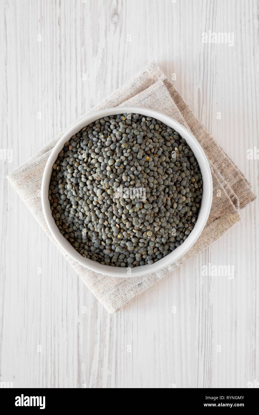 Overhead view, dry green french lentils in gray bowl over white wooden ...