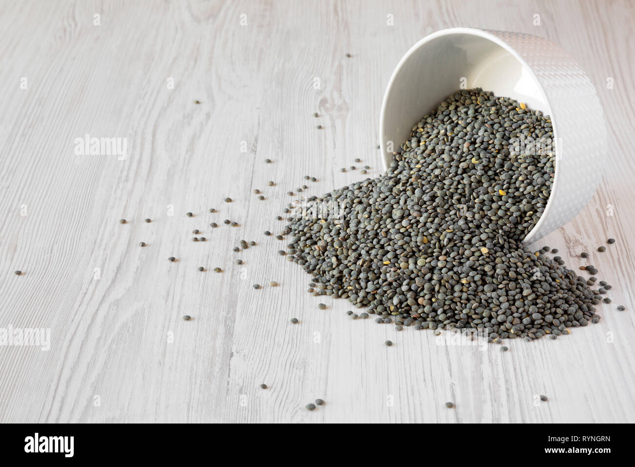 Green french lentils in gray bowl over white wooden background, side ...