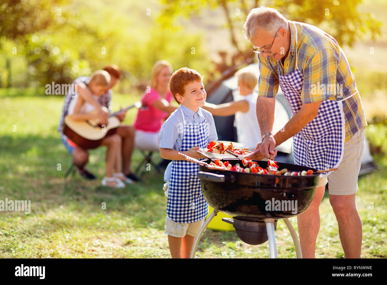 smiling grandfather giving grandson grilling meat for diner Stock Photo ...