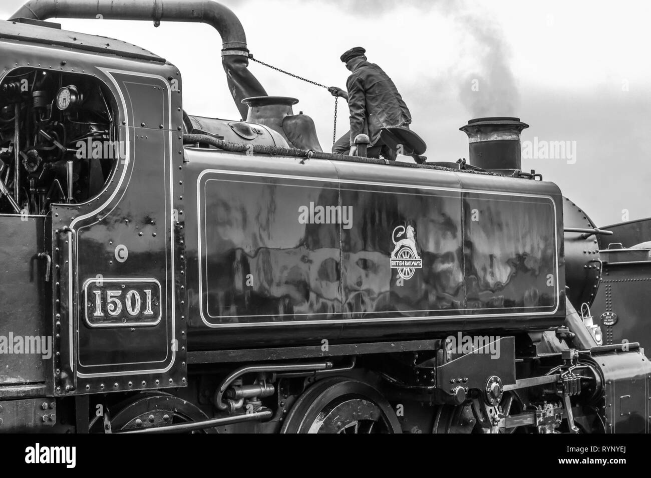 Black & white, side view close up of vintage UK steam locomotive in sidings taking on water ...