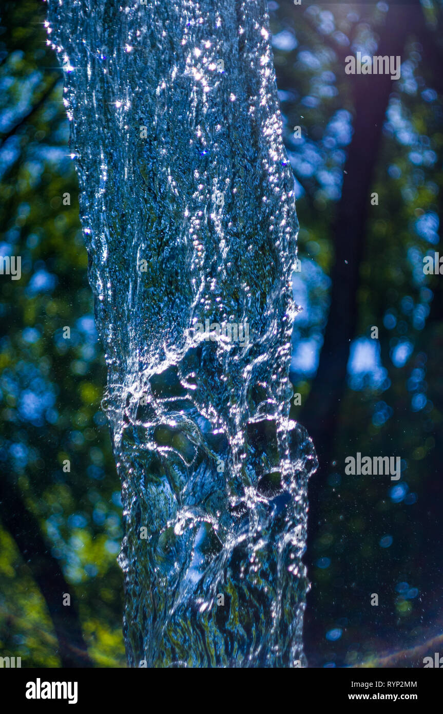 transparent falling water vertical flows against a blue sky and green ...