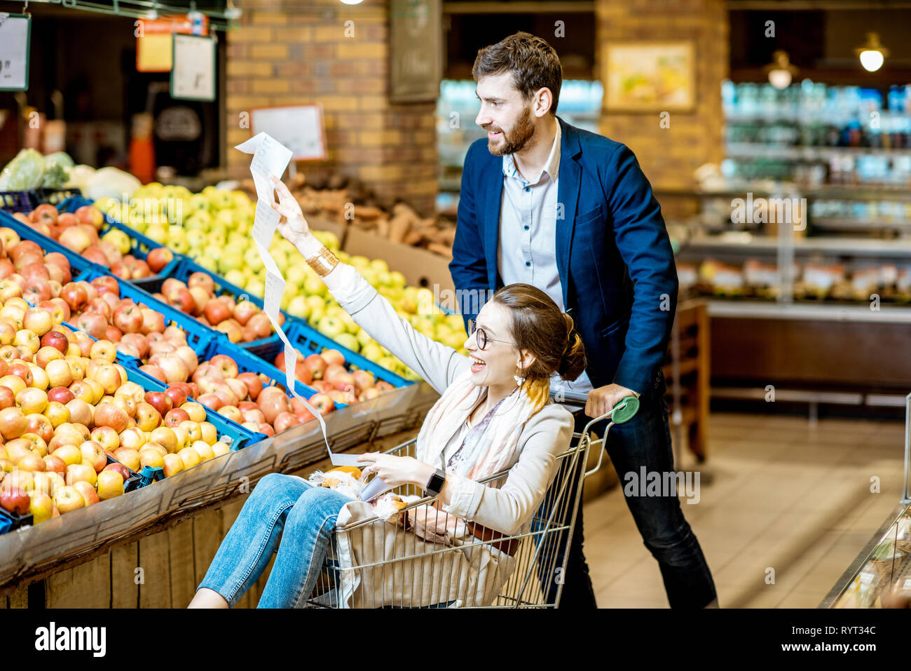 Man and woman having fun while riding in the cart with shopping list in ...