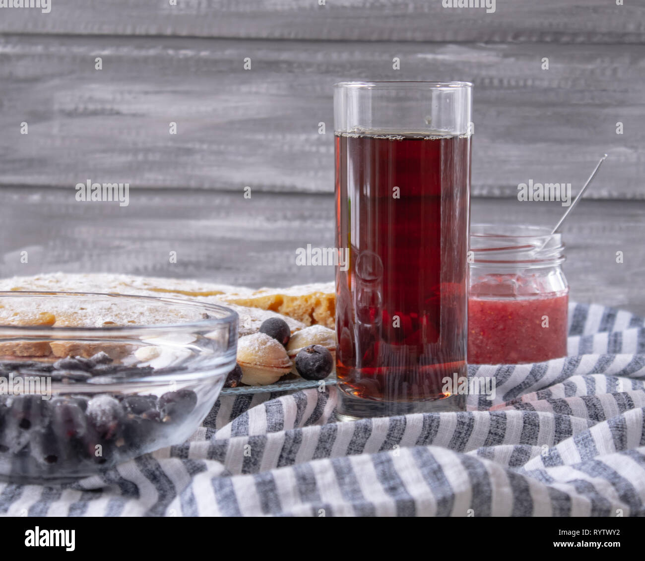 Red juice in a glass next to a bowl of cookies and a jar of jam, close ...