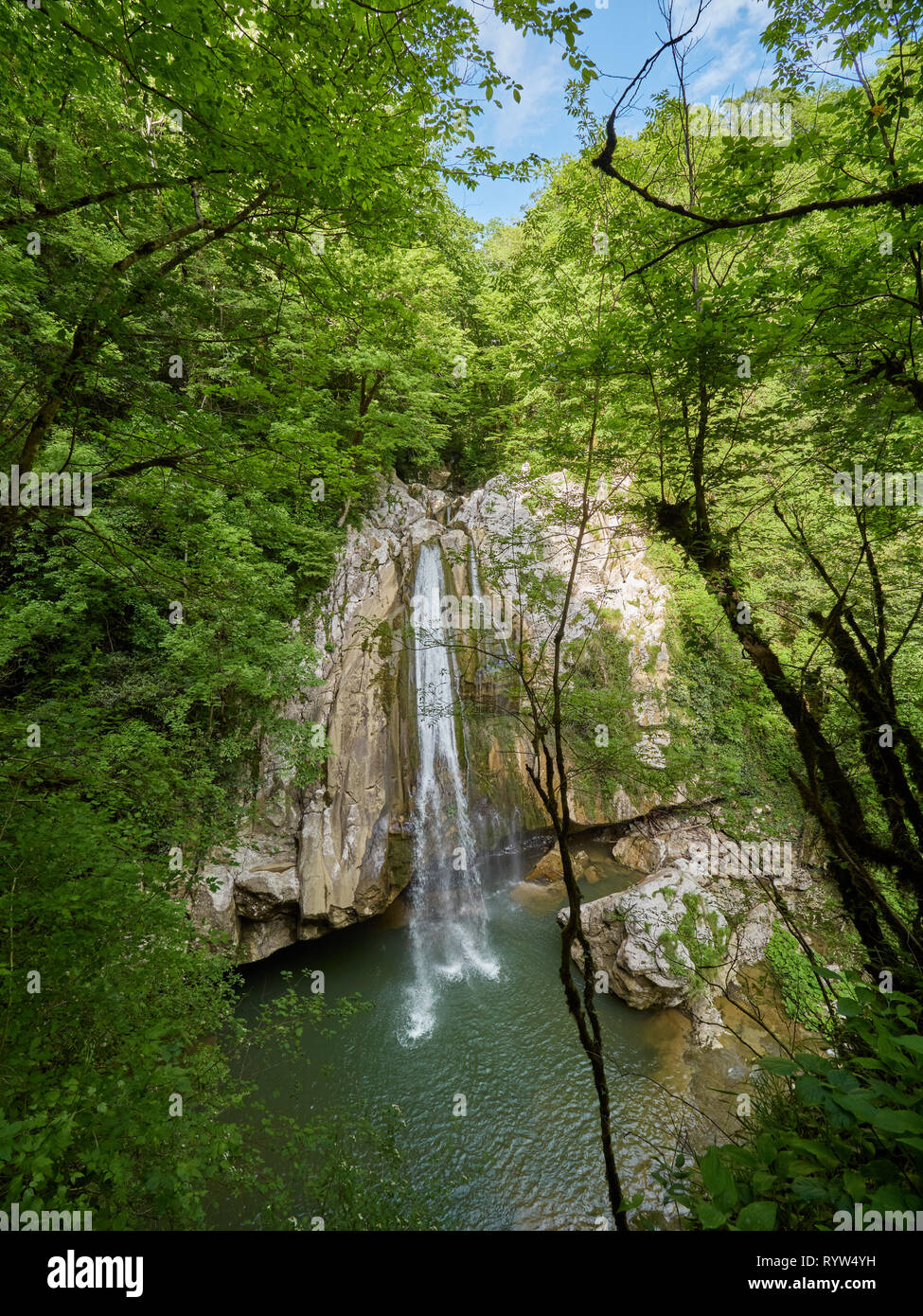 A high waterfall falls from a cliff into a clear lake. The waterfall is ...
