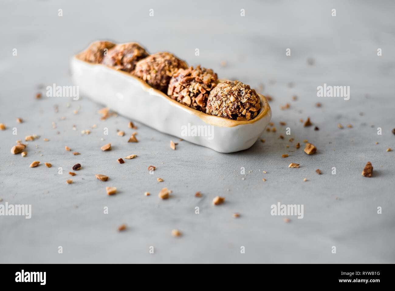 Raw bliss balls with chopped hazelnuts in an oval bowl on textured ...
