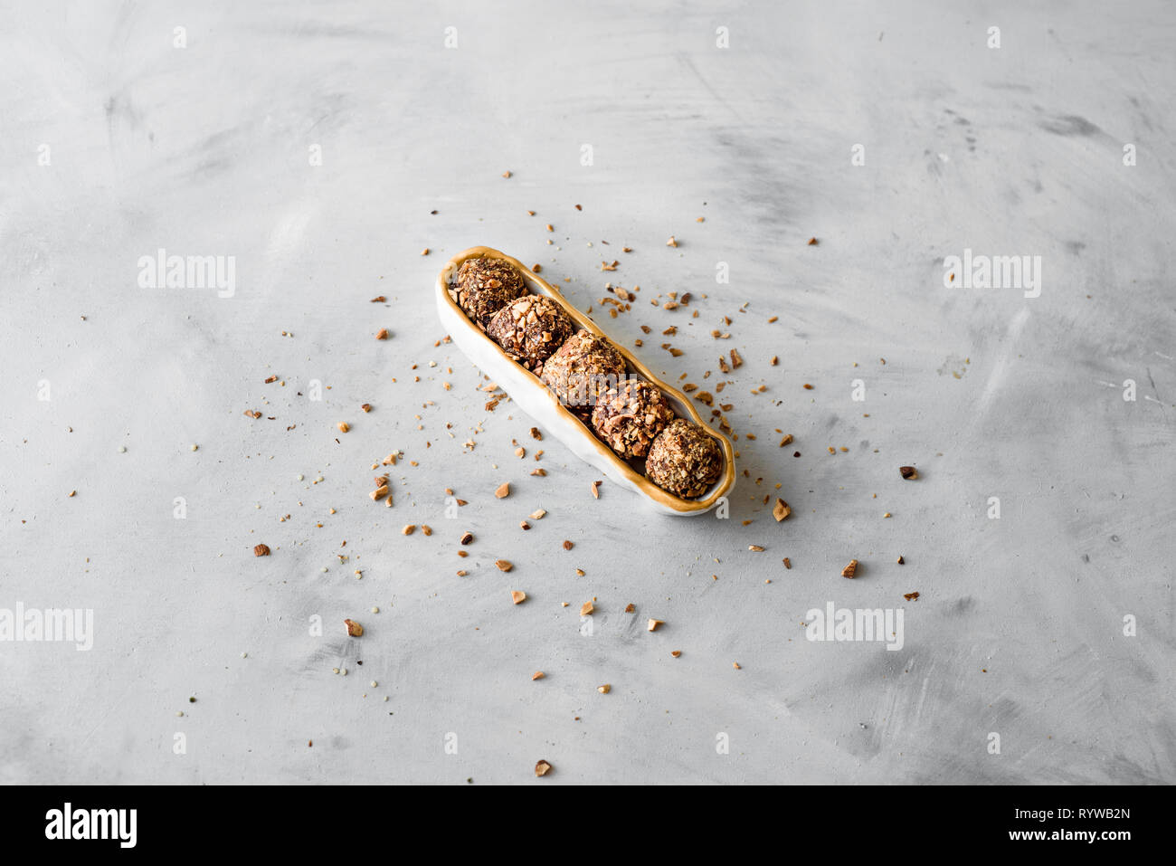 Raw bliss balls with chopped hazelnuts in an oval bowl on the textured ...