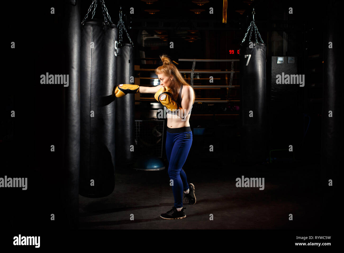 Blonde in boxing gloves trains near black punching bag Stock Photo - Alamy