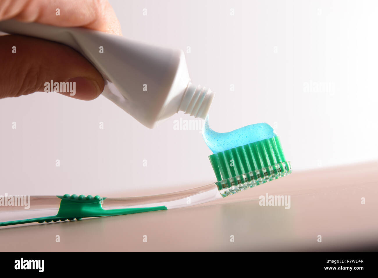 Hand with tube putting toothpaste in a green brush on a wooden table ...