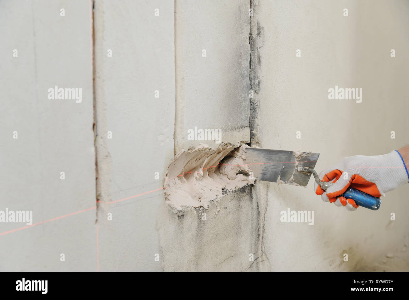Installing electrical socket box. A worker puts plaster into the hole ...