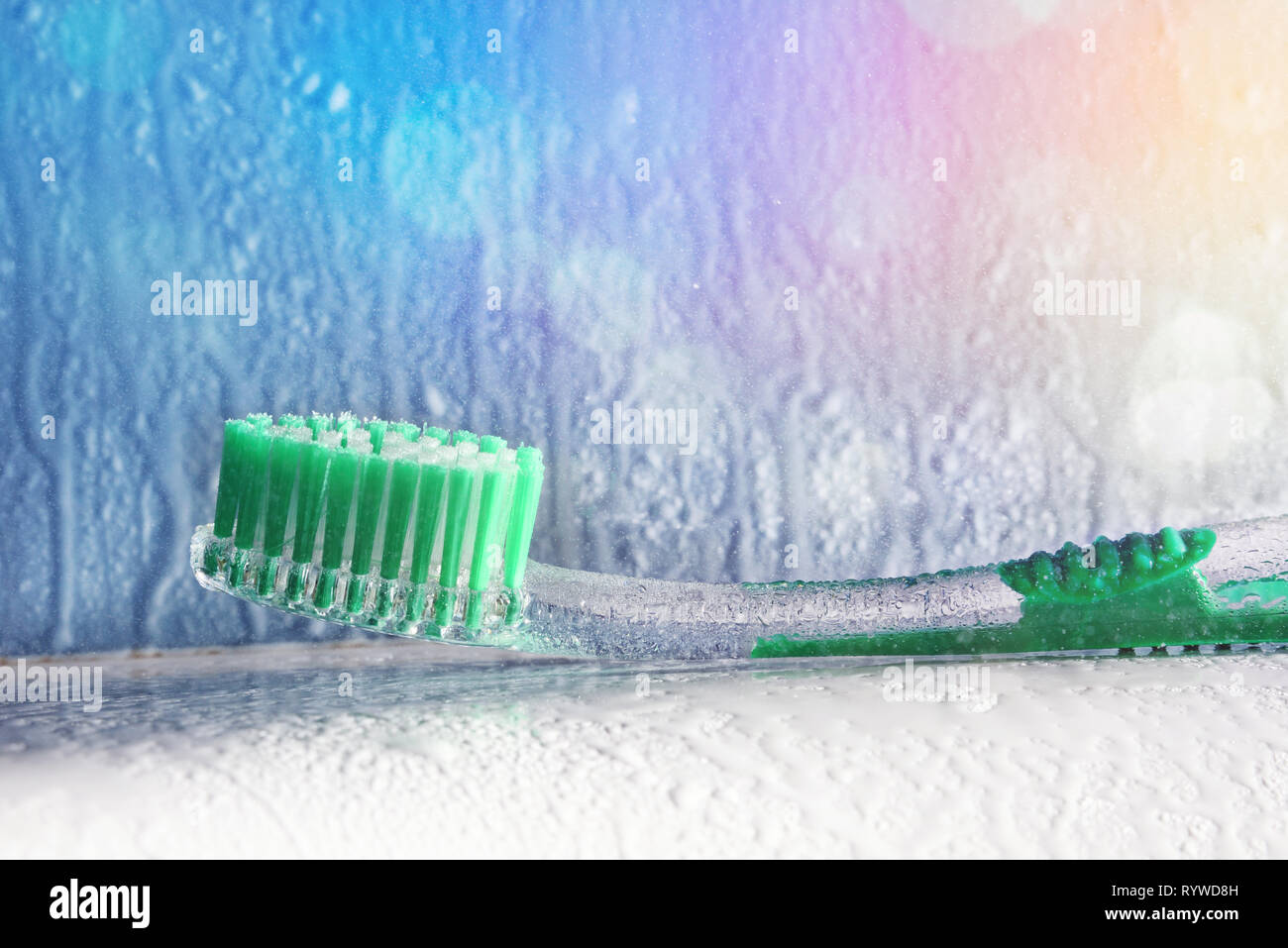 Green transparent toothbrush on a wet white wash with water spray with ...