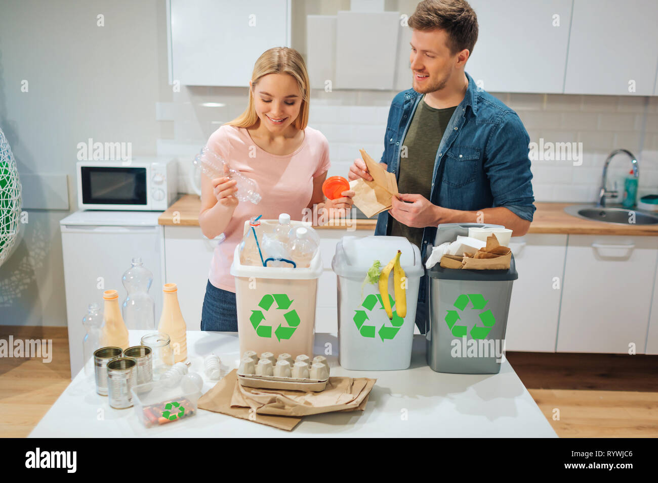 Waste sorting at home. Smiling young couple putting plastic, paper ...