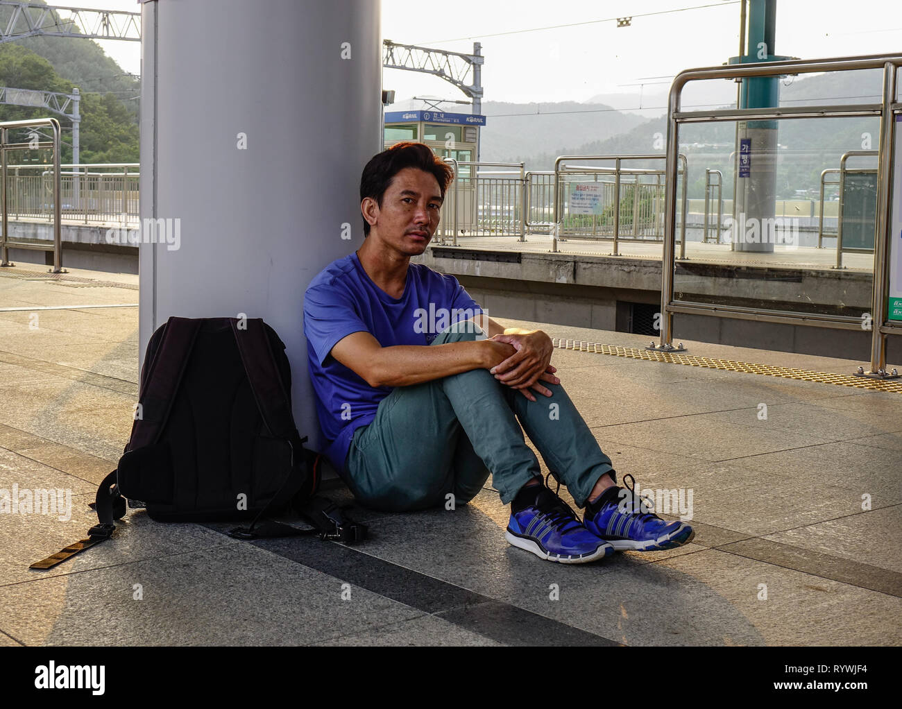 A tired man sitting and waiting the train at railway station in sunset ...