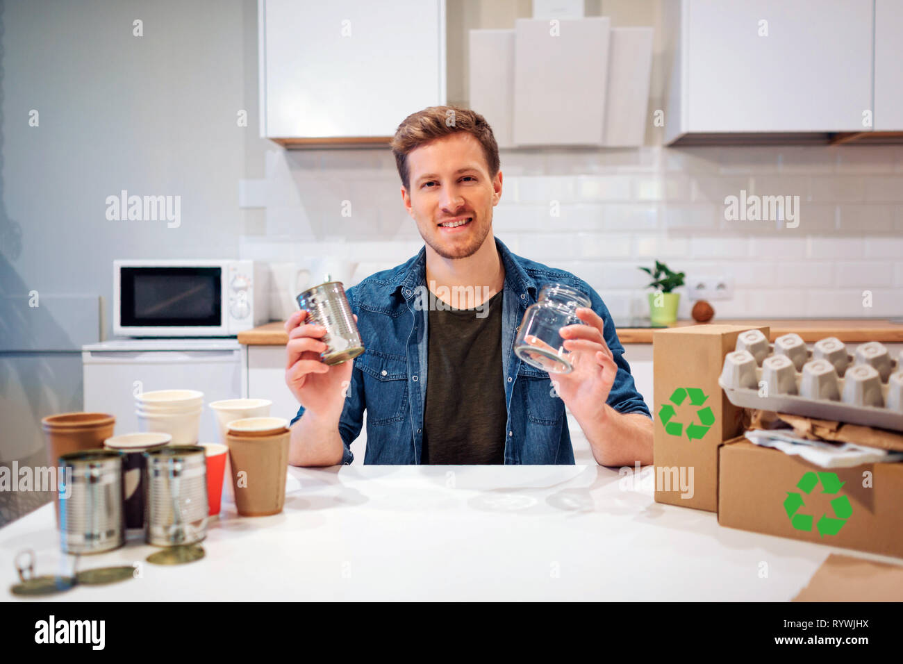Recycling. Young smiling man is sorting empty glass bottles and metal ...