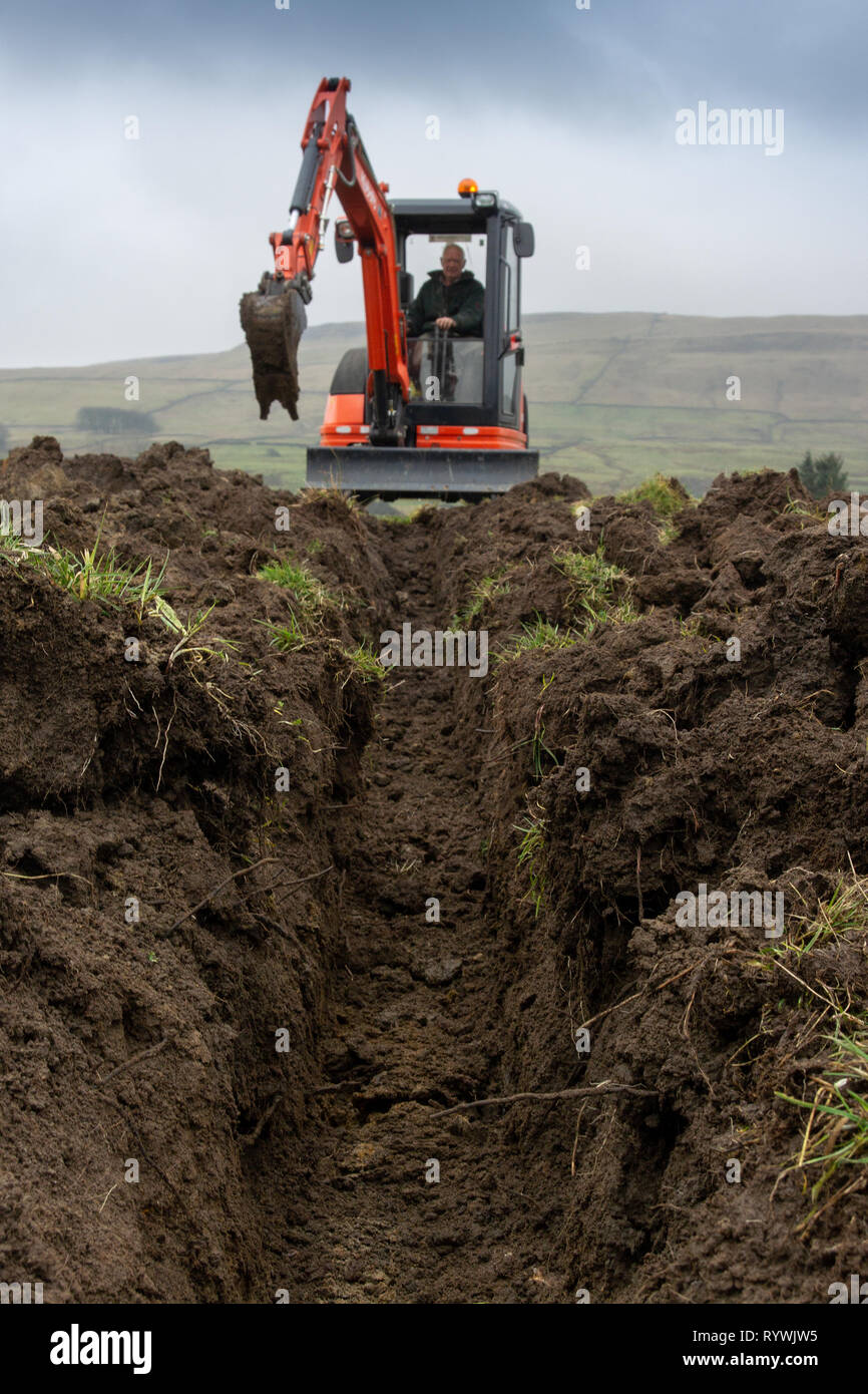 Digging a trench across a field to install a water supply to a field ...