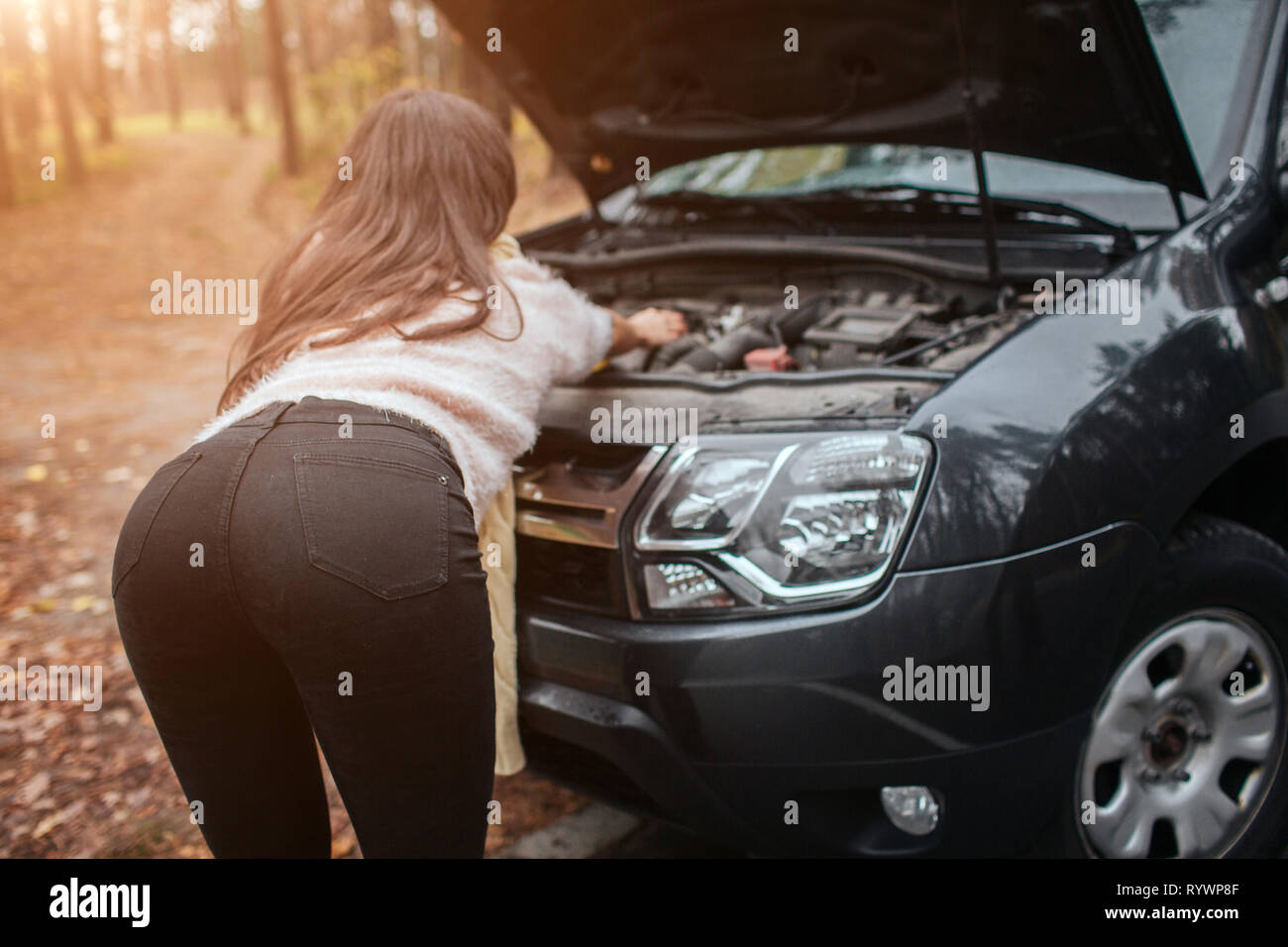 Confused young woman looking at broken down car engine car repair on ...
