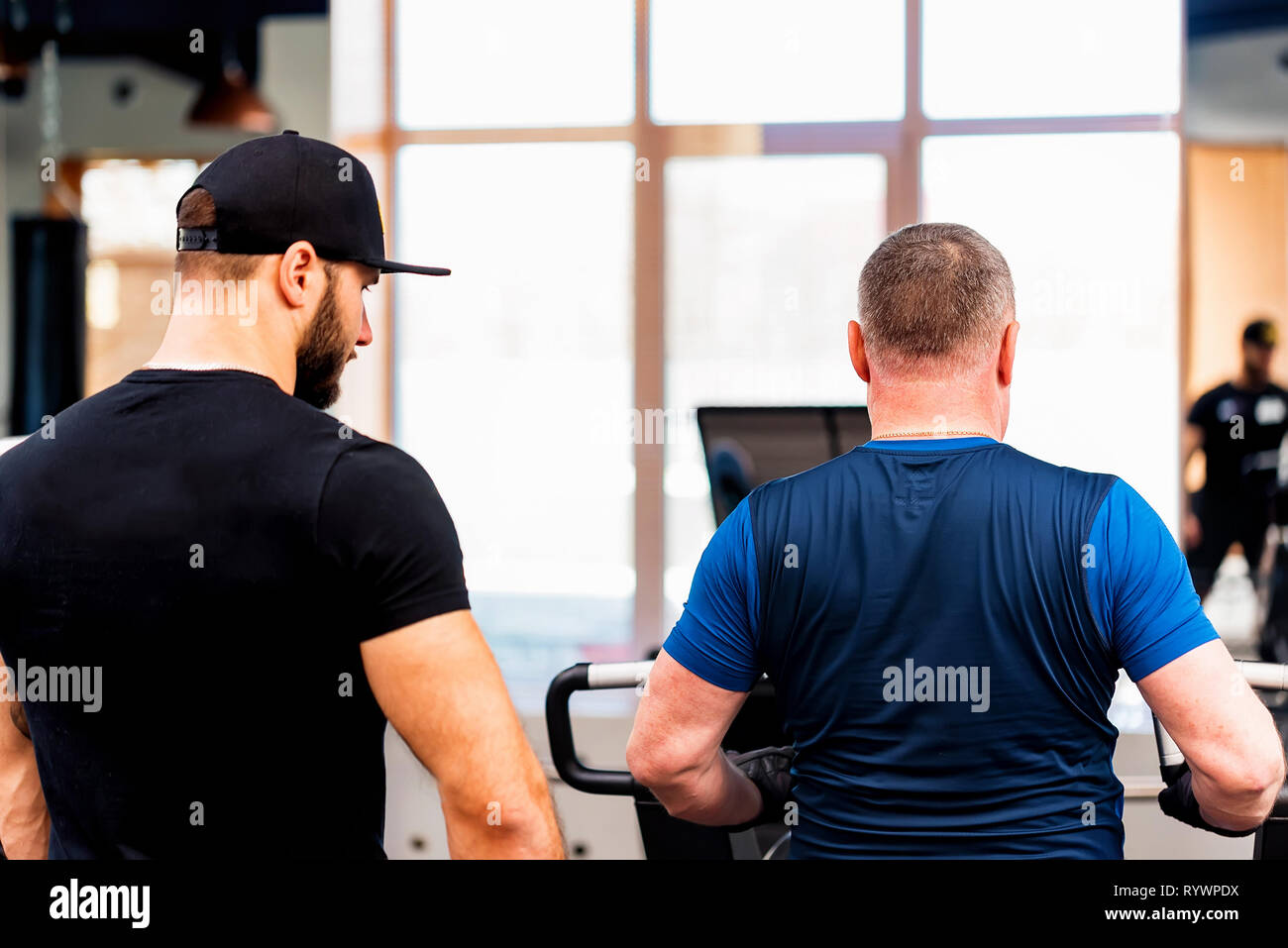 Back view personal trainer coaching male sportsman on machine in modern ...