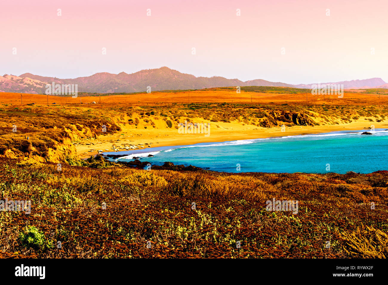 Overlooking fields and blue sea with mountains beyond under pastel pink ...
