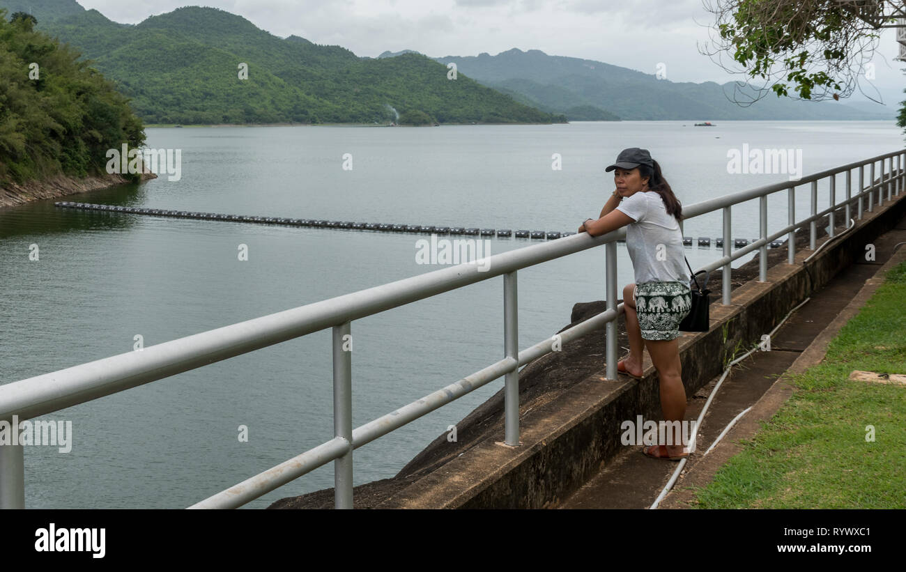 Asian woman leaning on railing looking at resevoir with mountains in ...