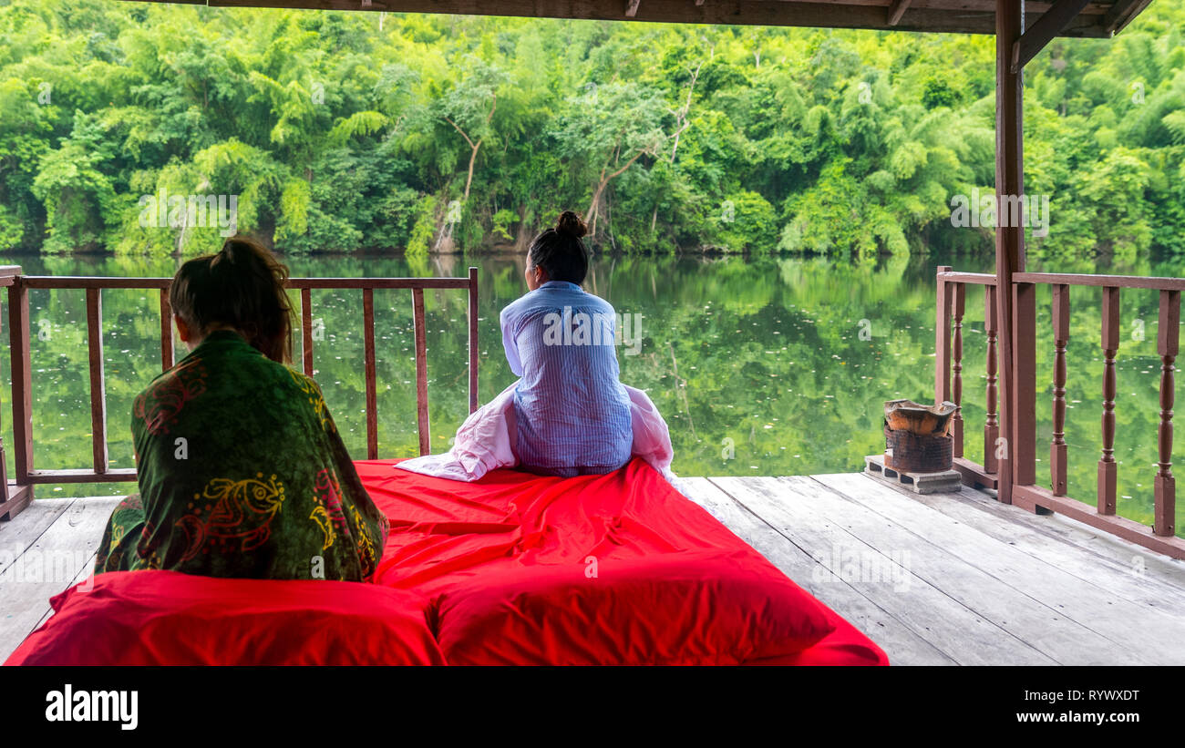 Mother and daughter sitting on red bed with reflection of trees in the ...