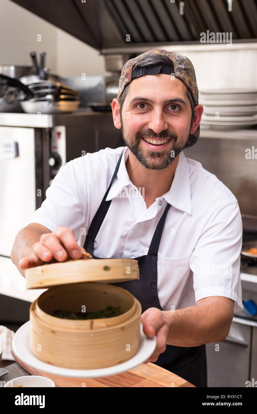 A happy chef in a restaurant kitchen holding a bamboo dim sum steamer ...