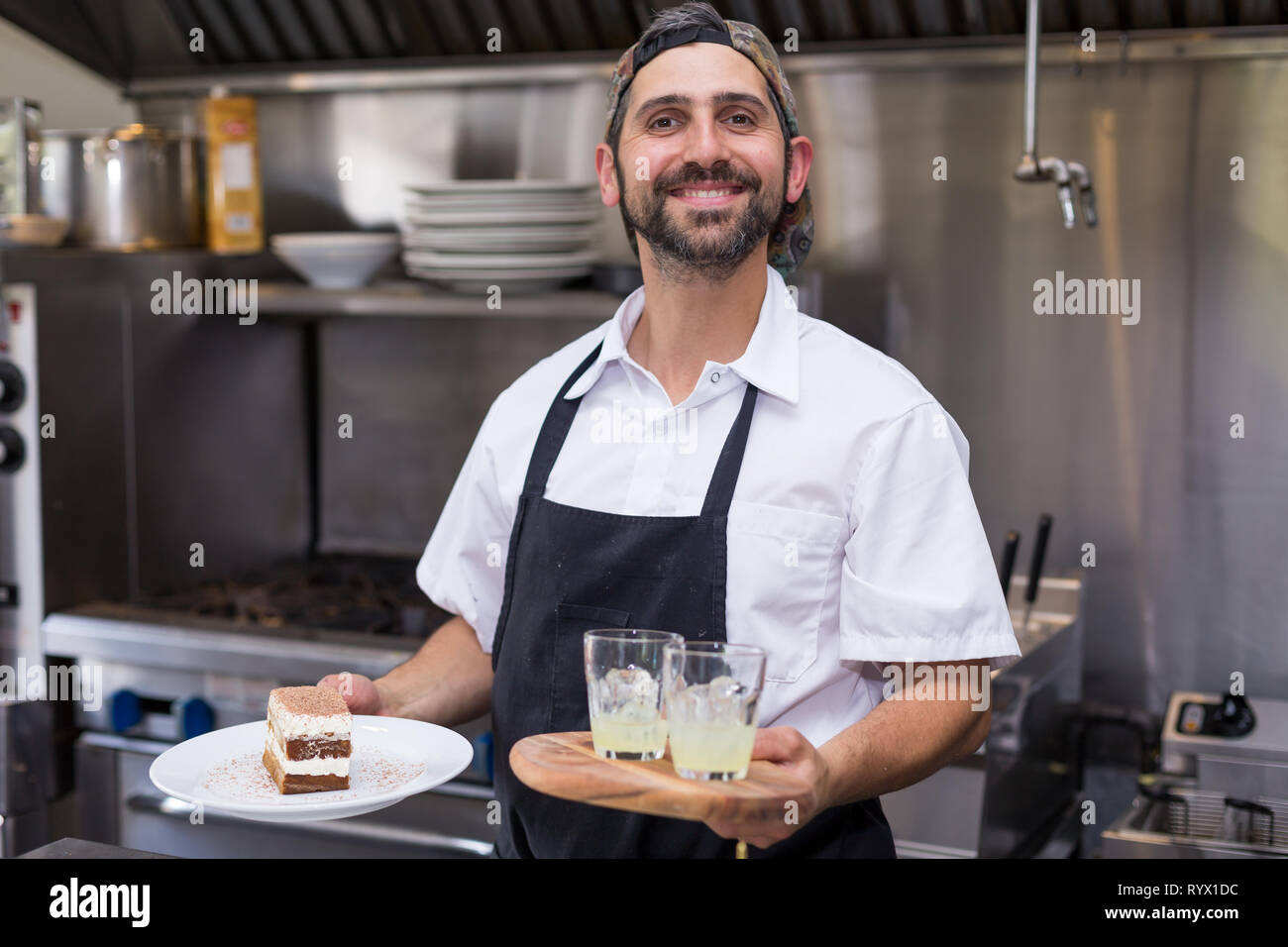 A happy smiling male chef holding tiramisu and limoncello in a ...