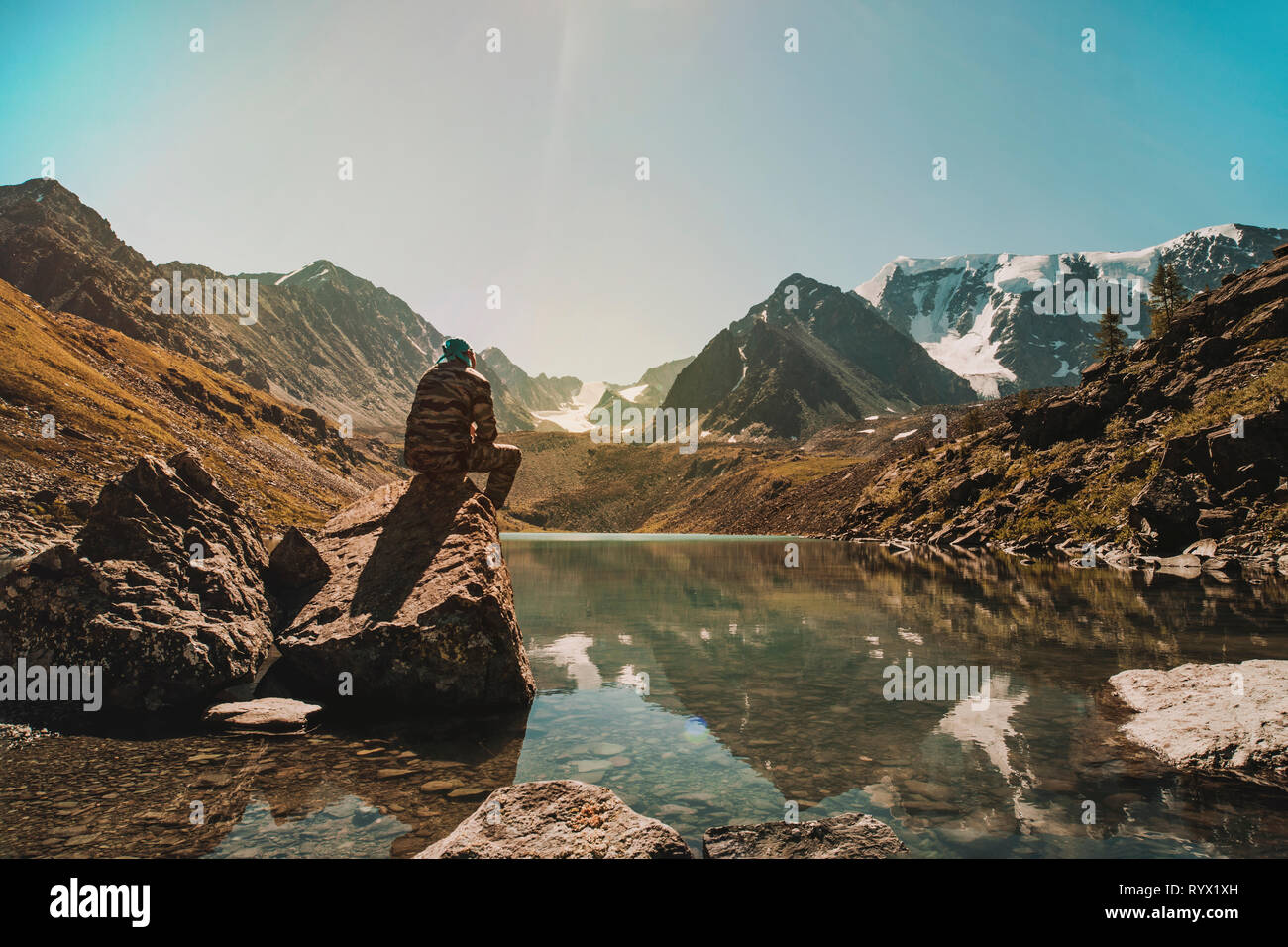 Young traveler man sits on a stone and admires the beautiful mountain ...