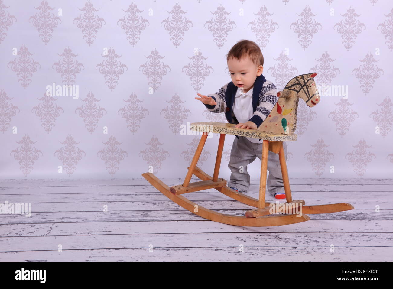 Little child trying to ride a small wooden rocking horse. Little boy ...