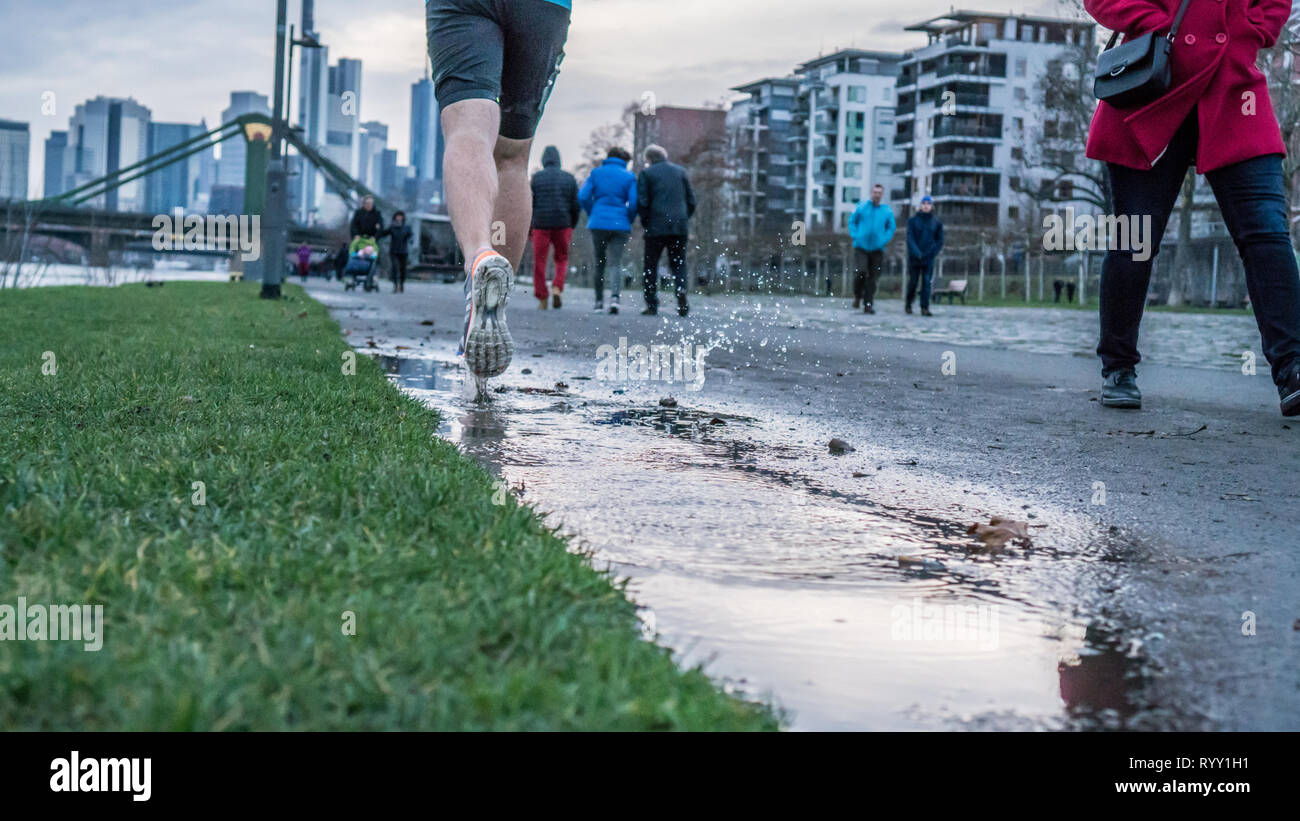 View of legs of a man running after rain along a river in a big city ...