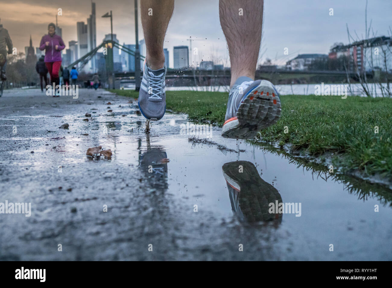 View of legs of a man running after rain along a river in a big city ...