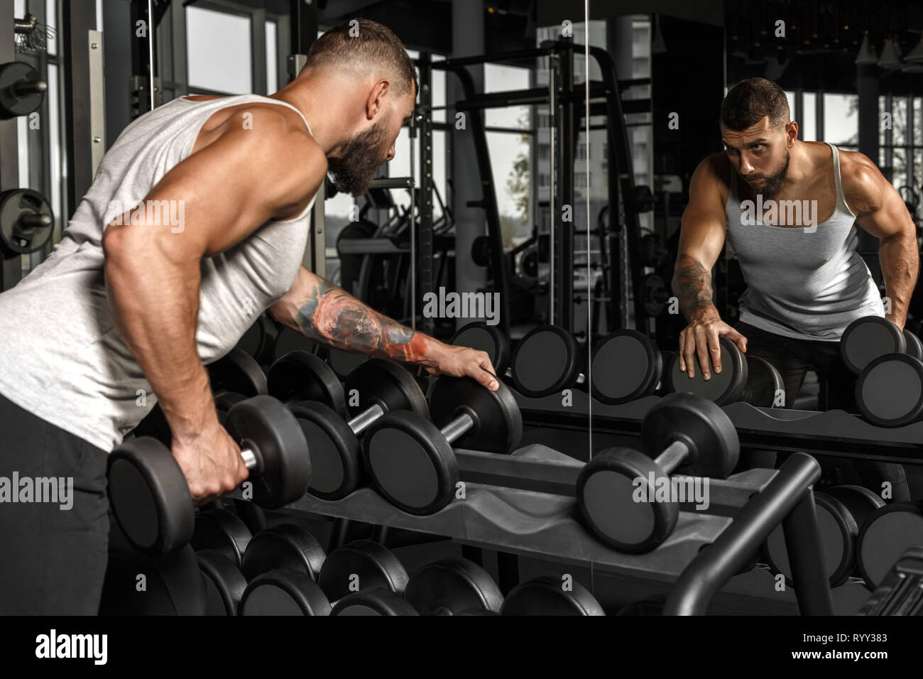 Bodybuilding. Bearded man exercising at gym with dumbbell looking at ...