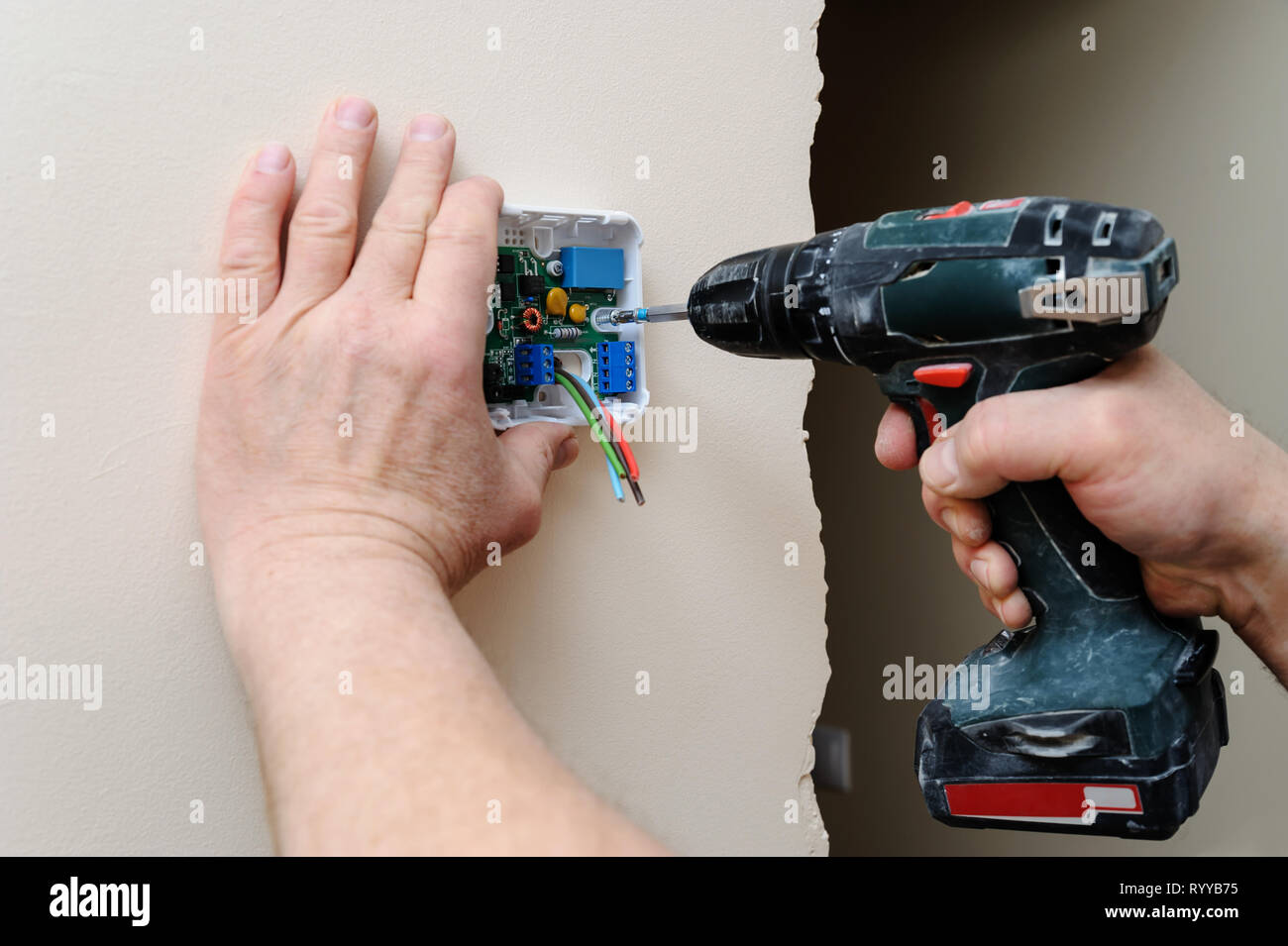Installing a programmable room thermostat. Man's hands attach device to ...