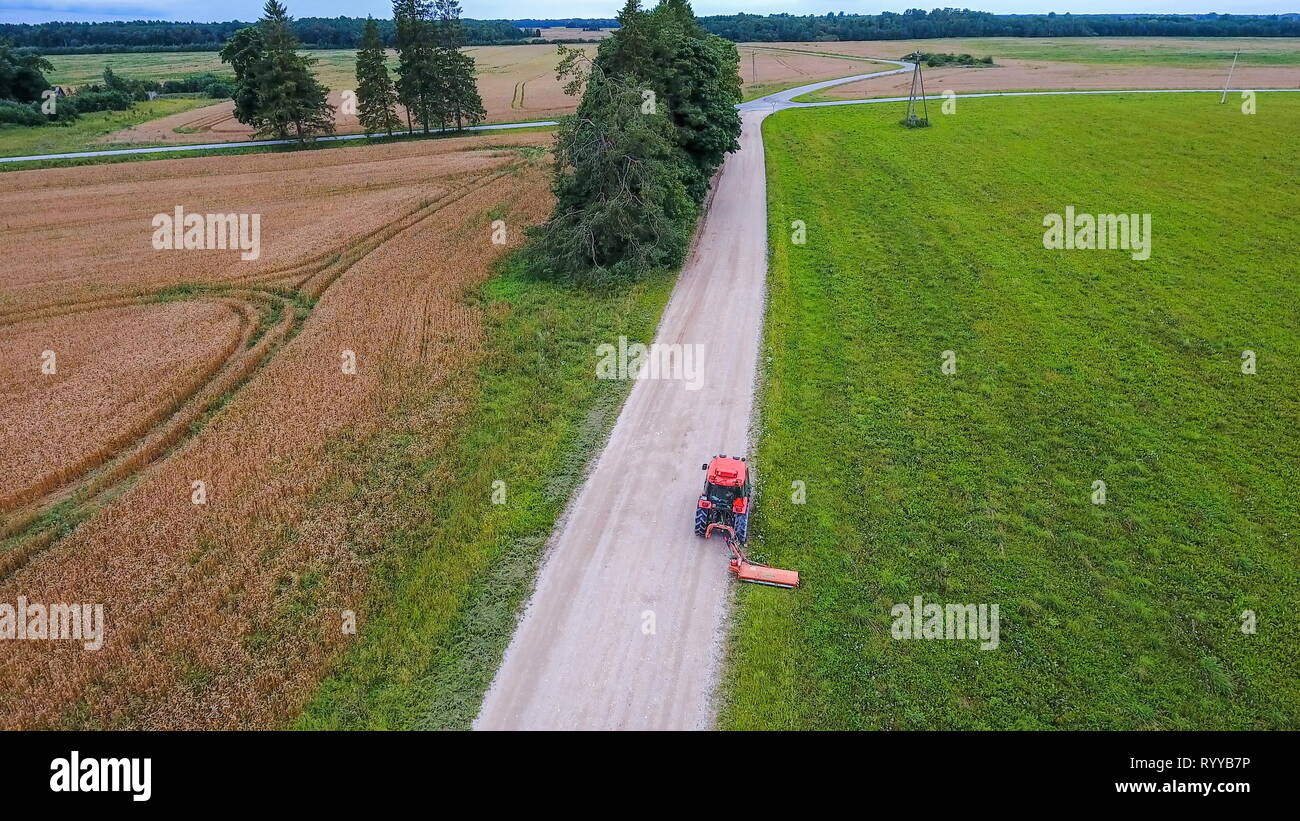 The big mower trimming the thick grasses on the wide field taken in an ...