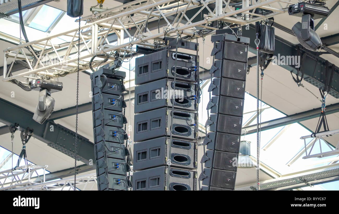 Lots of black amplifiers hanging on the ceiling of a concert stage with ...