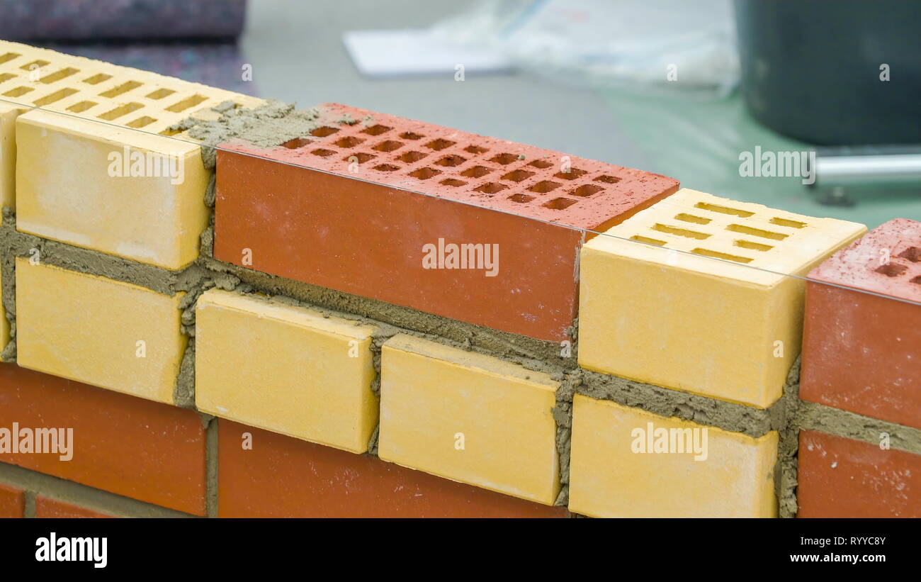 A man using a ruler to make sure the bricks are aligned then filling up ...