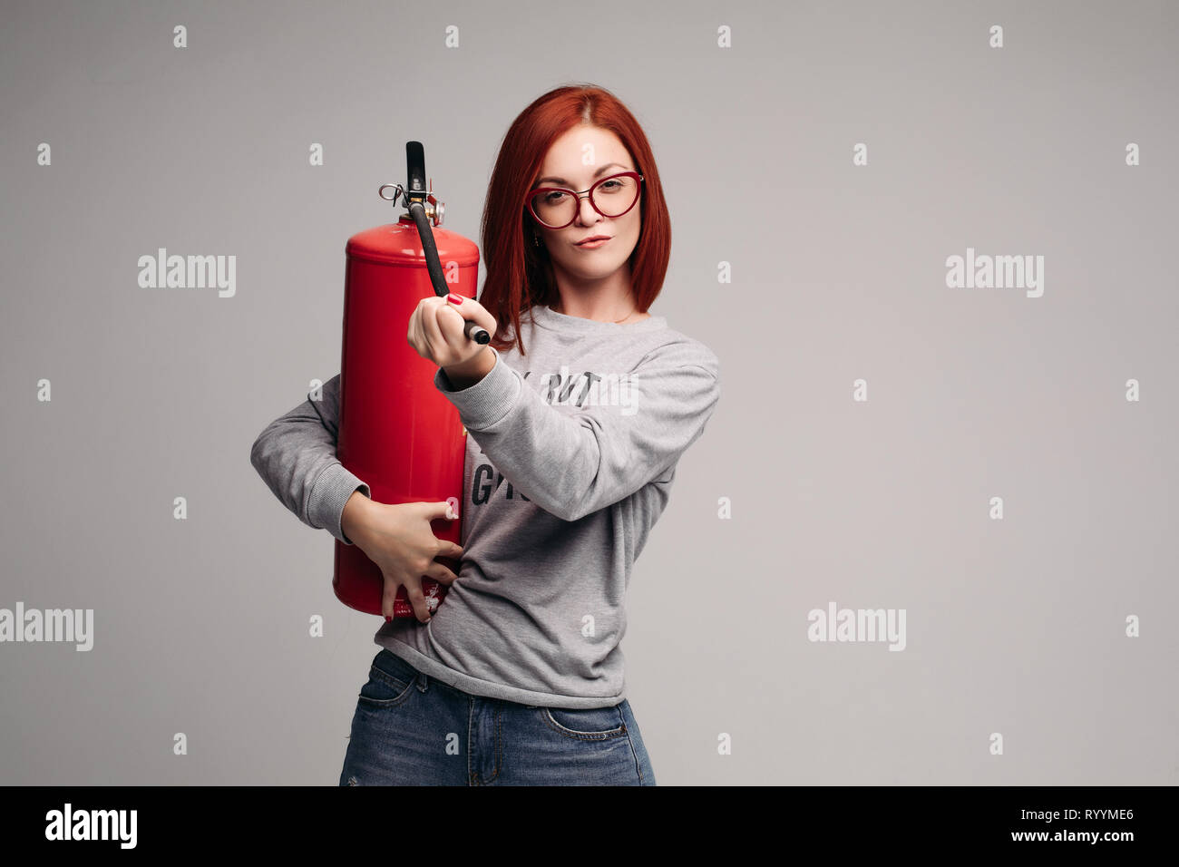 A woman with red hair in the Studio holding a fire extinguisher. An ...