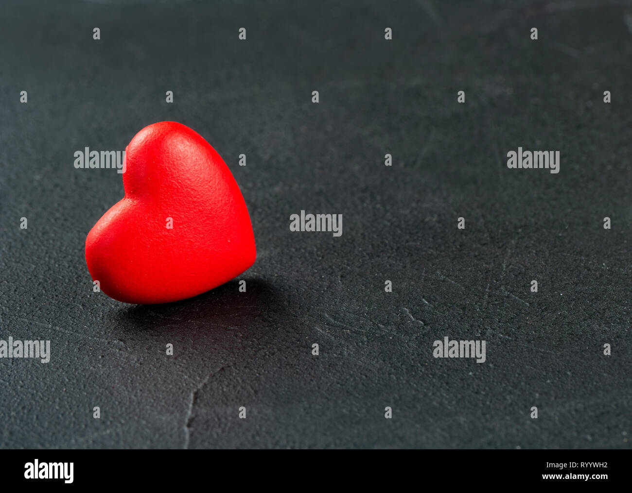 One red plastic heart on a dark concrete background Stock Photo - Alamy