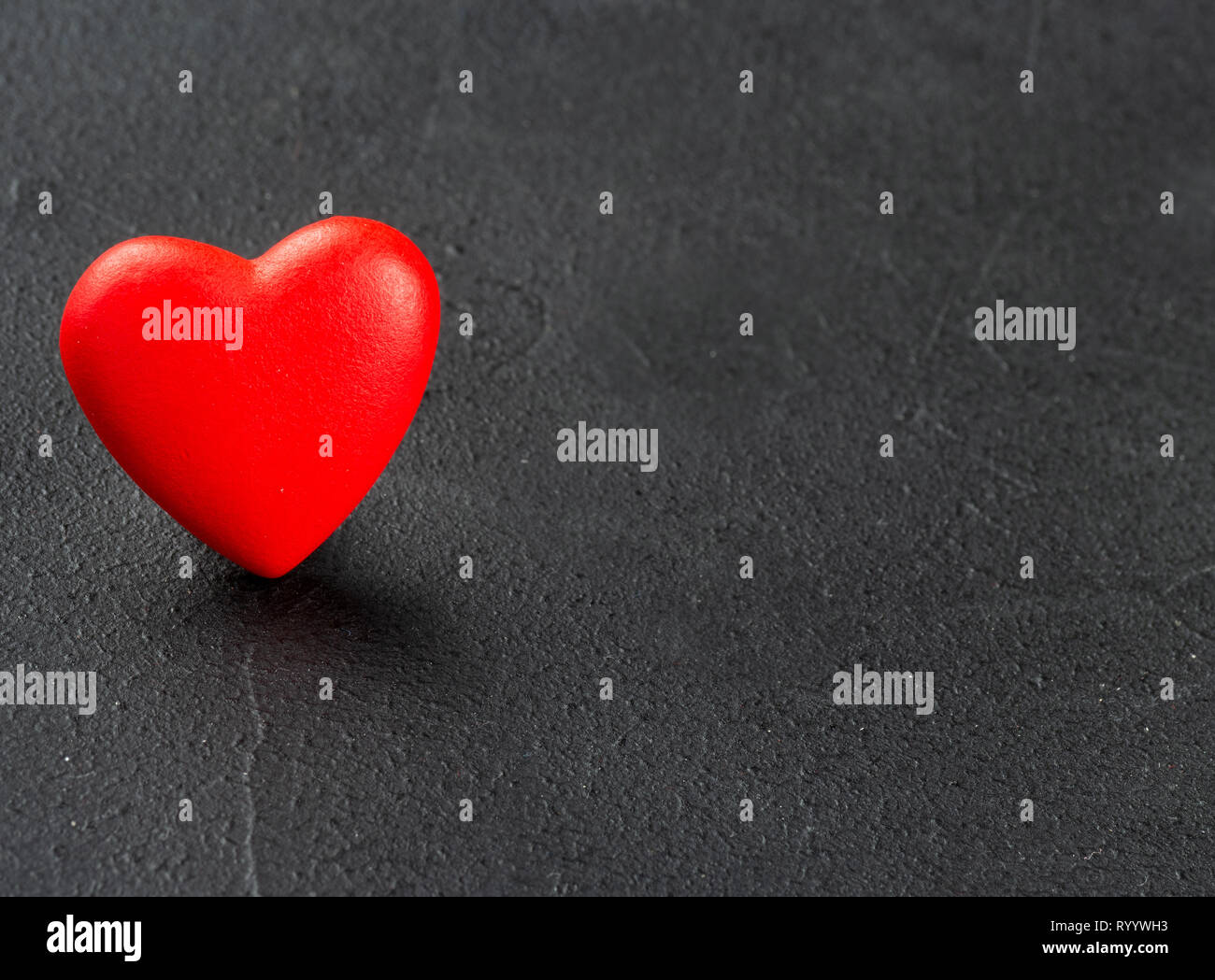 One red plastic heart on a dark concrete background Stock Photo - Alamy