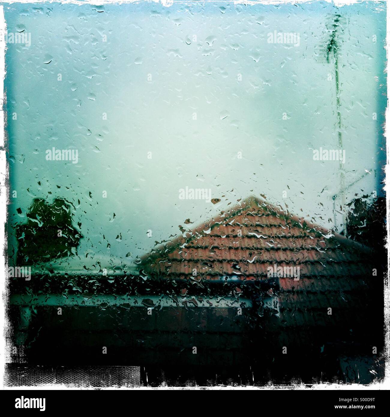Looking out though a window at rain seeing rain drops and roof top ...