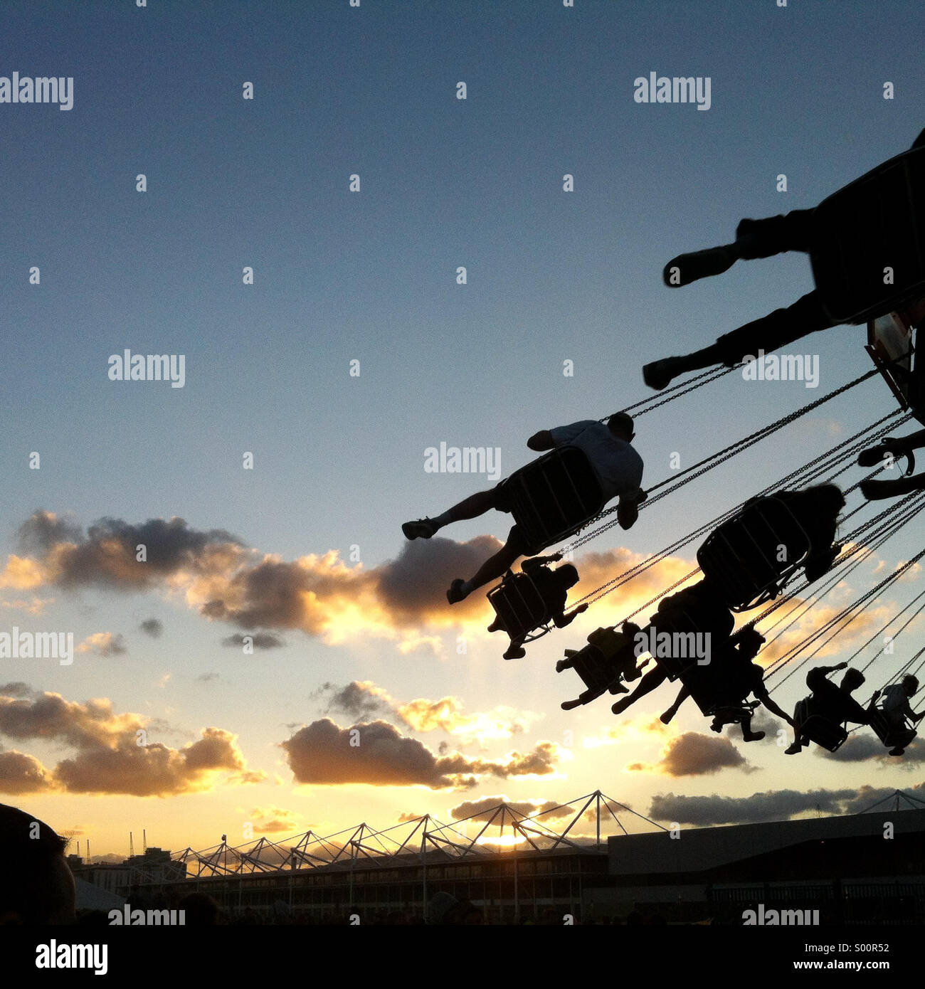 Silhouette of people on a fairground ride against golden clouds as the ...
