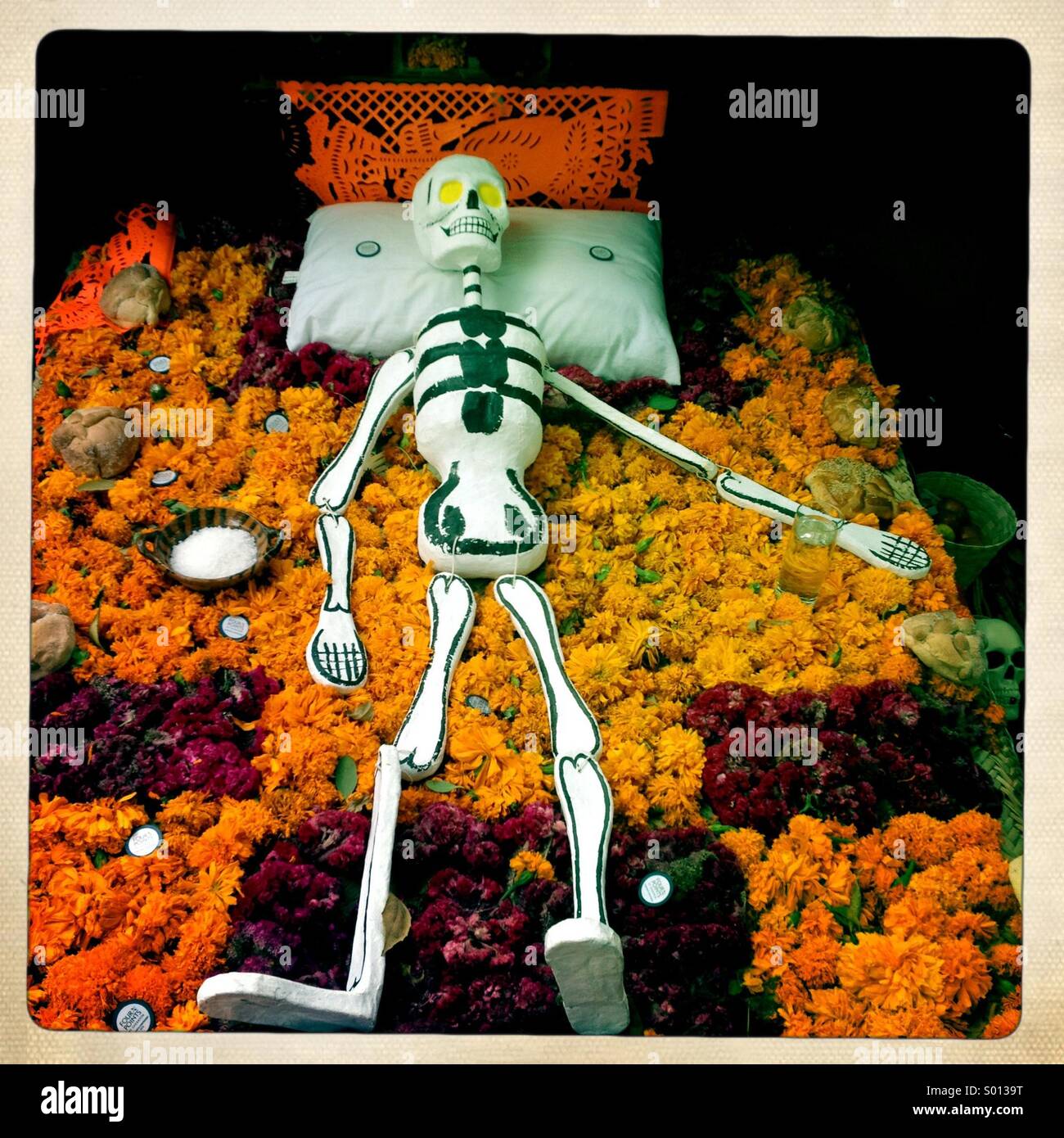 A paper mache skeleton sleeping in a bed of marigold flowers decorates ...
