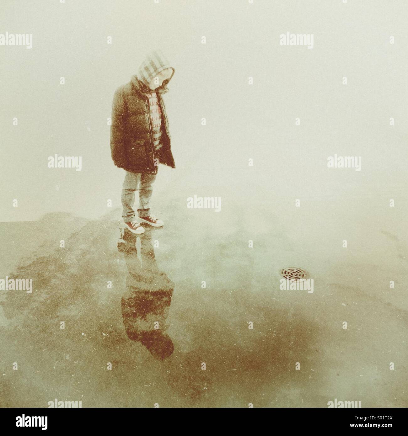 Young boy stood in a puddle looking at his reflection before the water ...