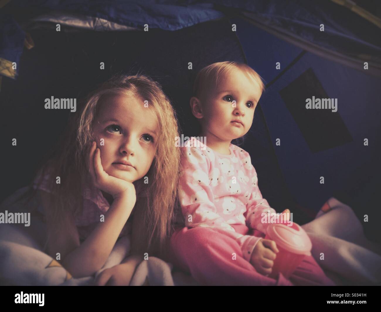Two sisters camping indoors and watching a bedtime movie Stock Photo ...