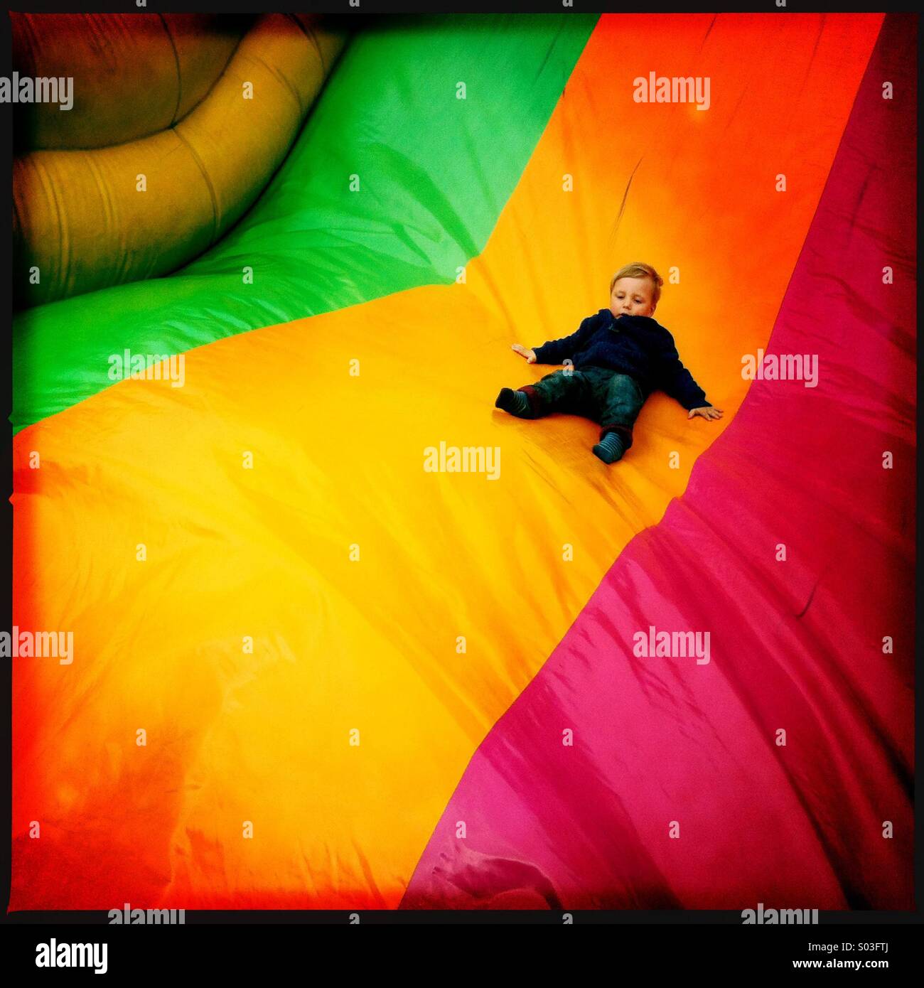 A two year old boy sliding down a large inflatable slide at a fun fair ...