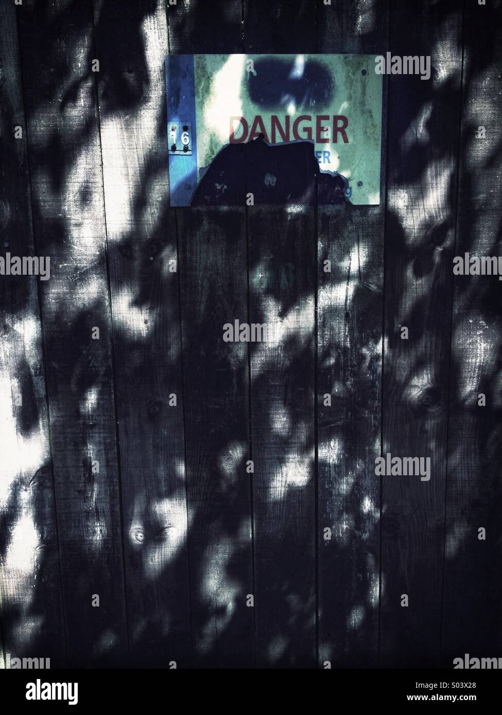 Damaged danger sign on shadow dappled fence Stock Photo - Alamy